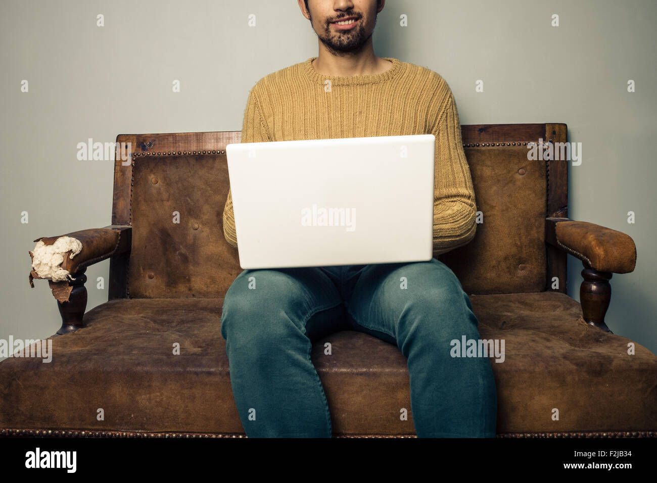 Young man sitting on sofa with laptop Stock Photo - Alamy