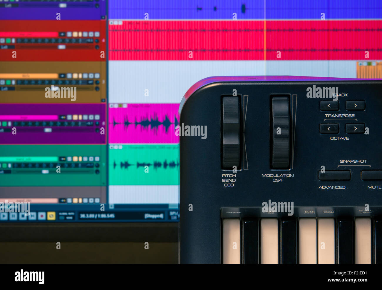 Midi keyboard and controller with faders and buttons. Waveforms in a DAW are visible in the ...