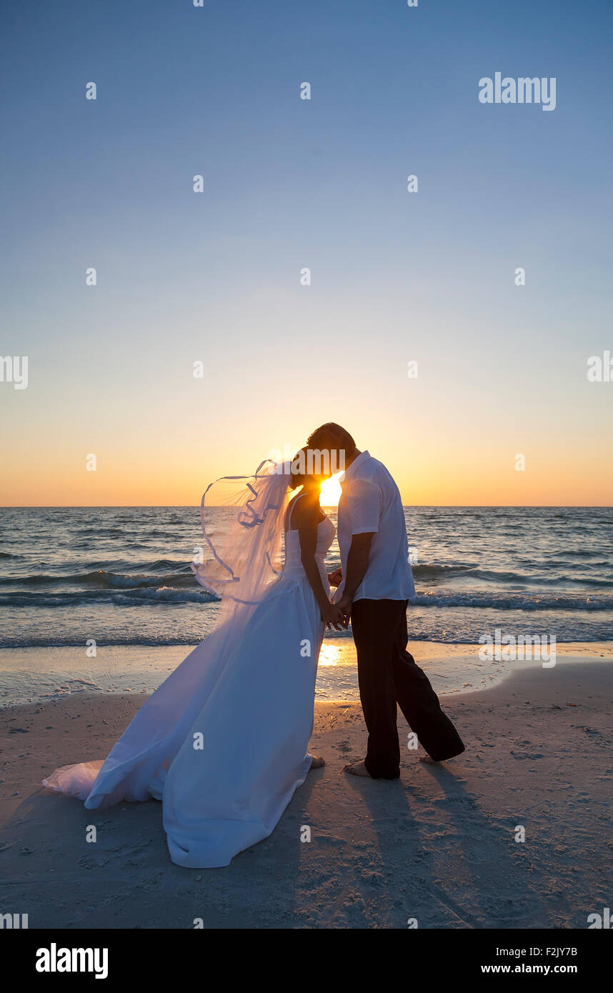 A married couple, bride and groom, kissing at sunset sunrise wedding on ...