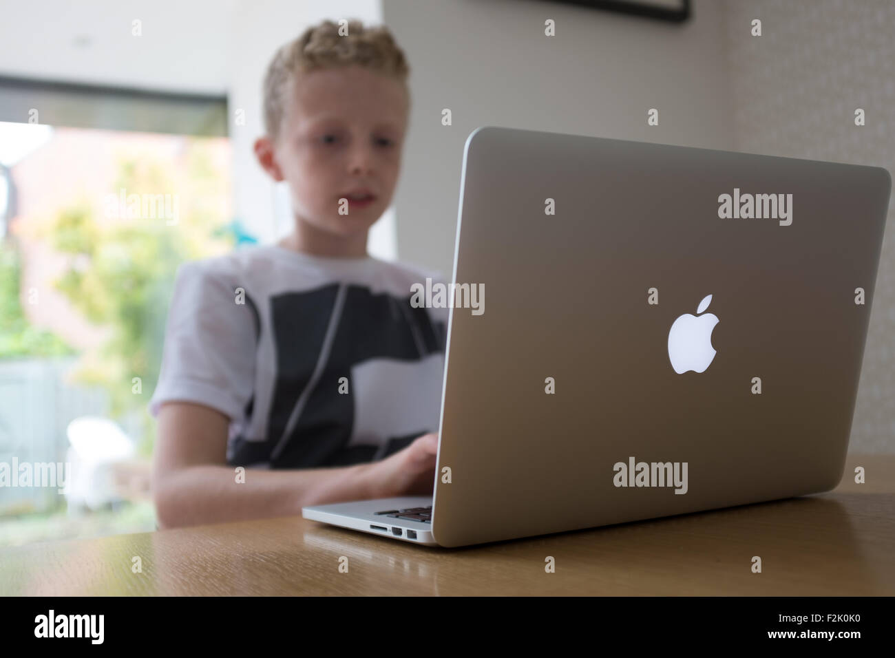 eleven year old boy doing his homework on a macbook laptop computer ...
