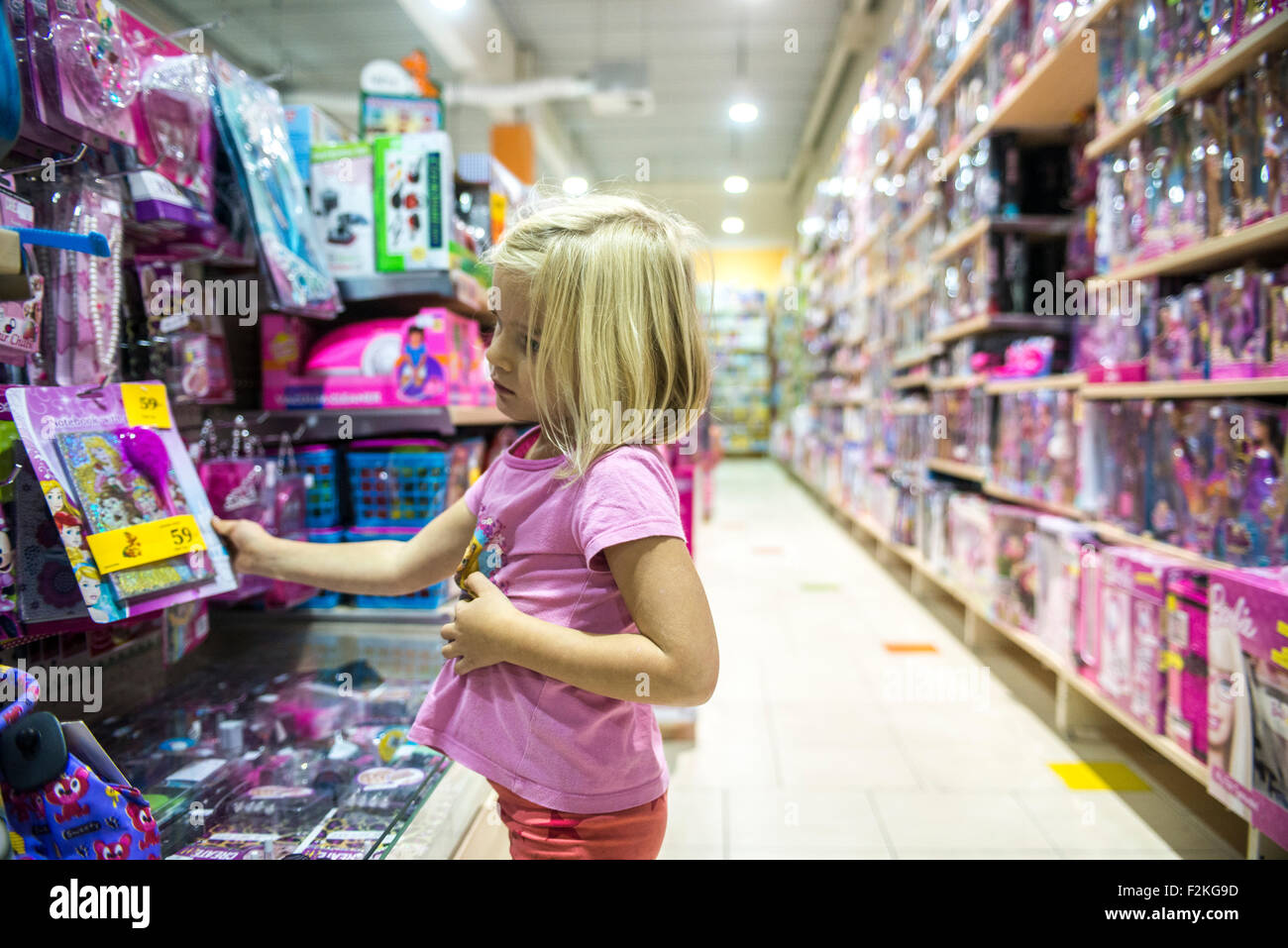 Little child blond girl choosing and shopping a toy in the toy store ...