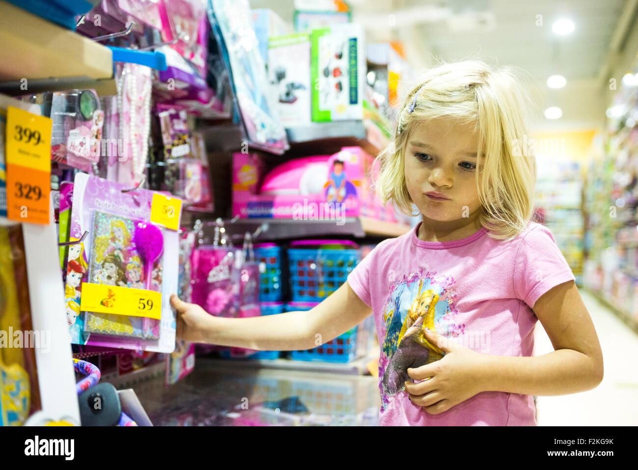 Little child blond girl choosing and shopping a toy in the toy store ...