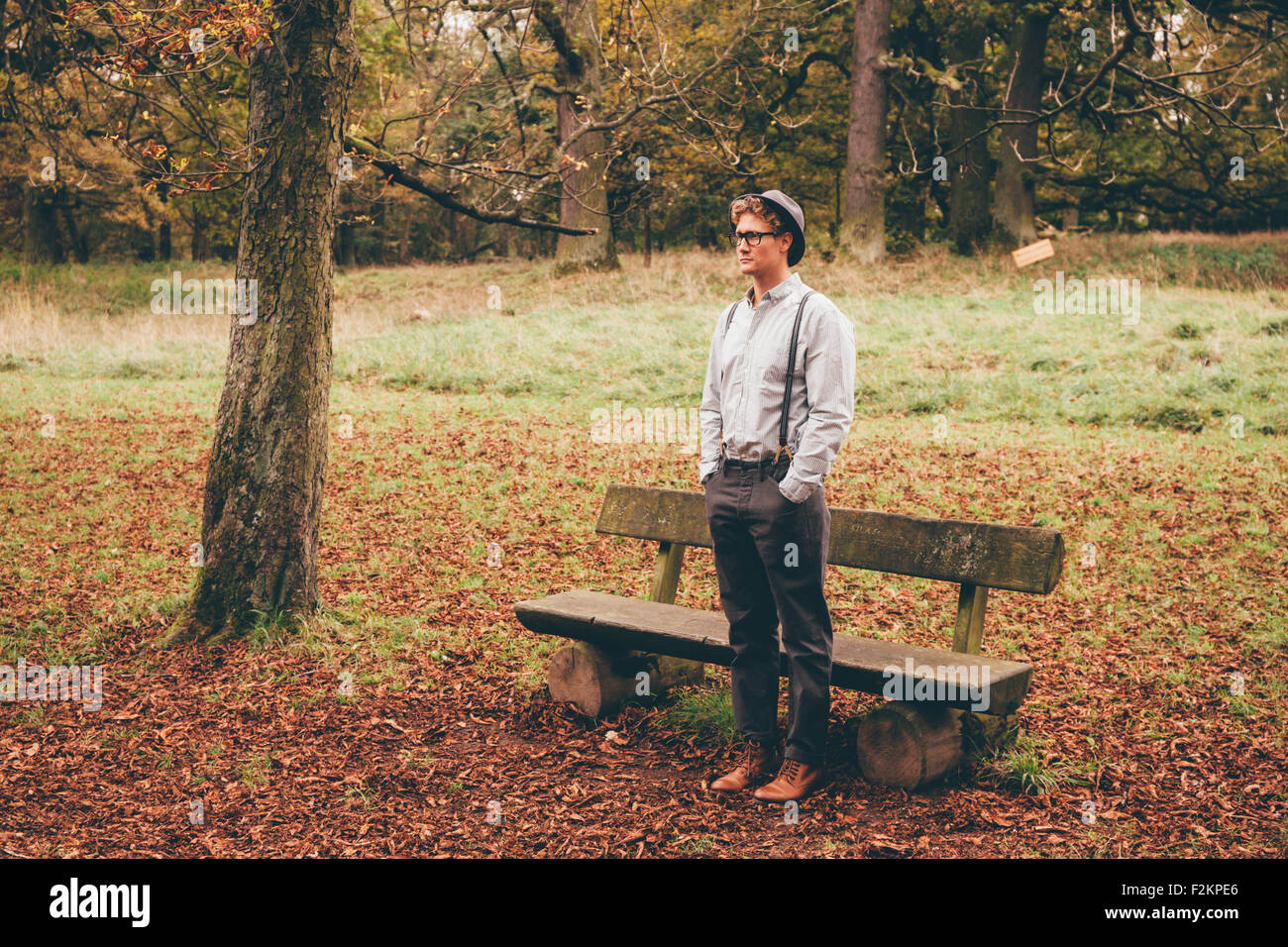 Young man standing in front of a bench in autumnal park looking at ...