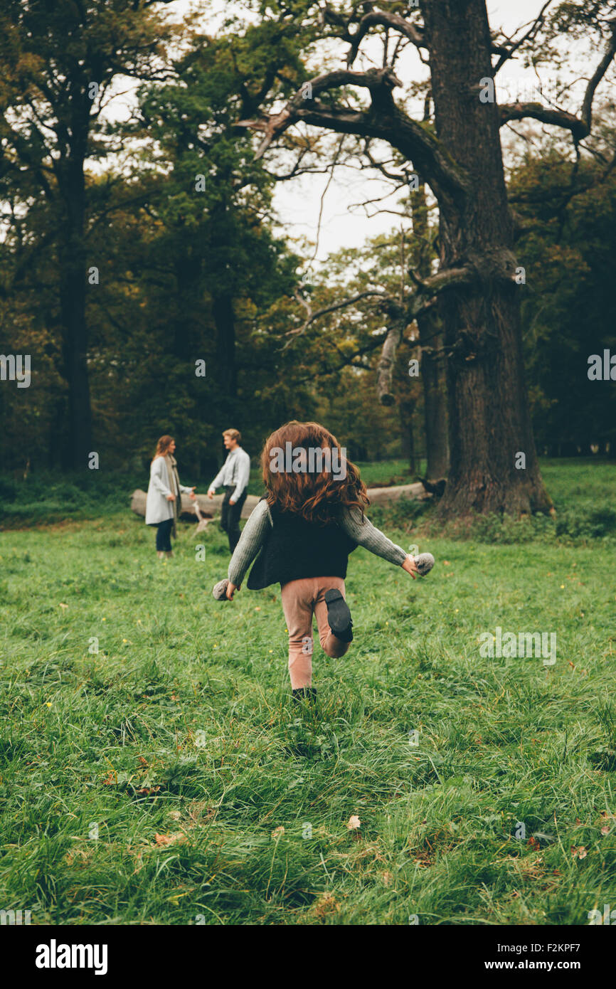 Back view of little girl running in a park while her parents standing ...