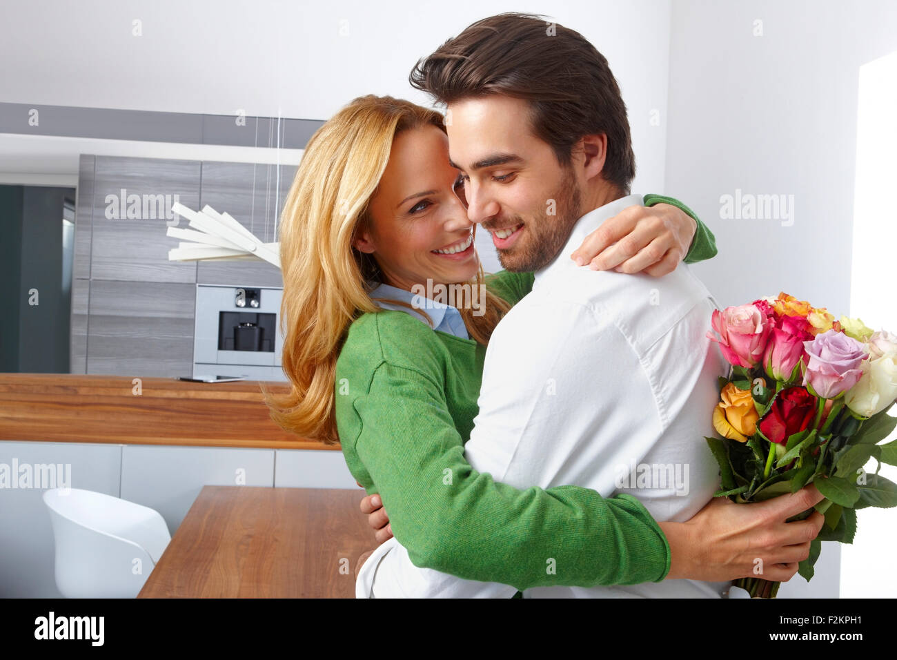 Young woman holding bunch of flowers hugging her boyfriend at home ...