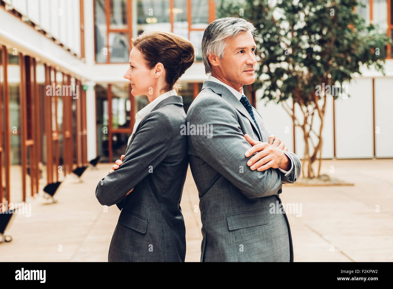 Mature corporate executives standing back to back with arms crossed ...