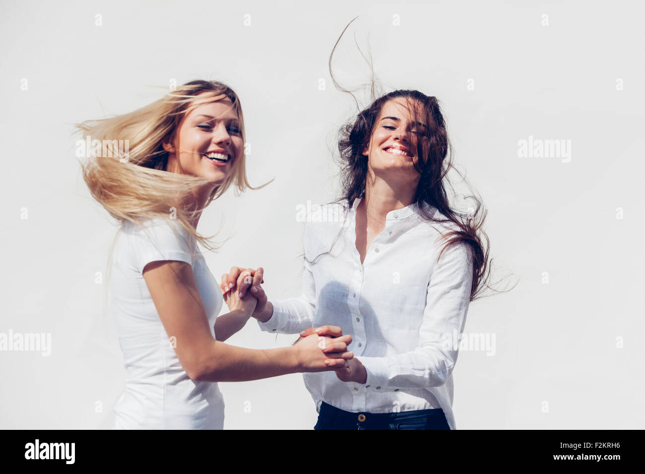 Two young women holding hands tossing her hair in front of white ...