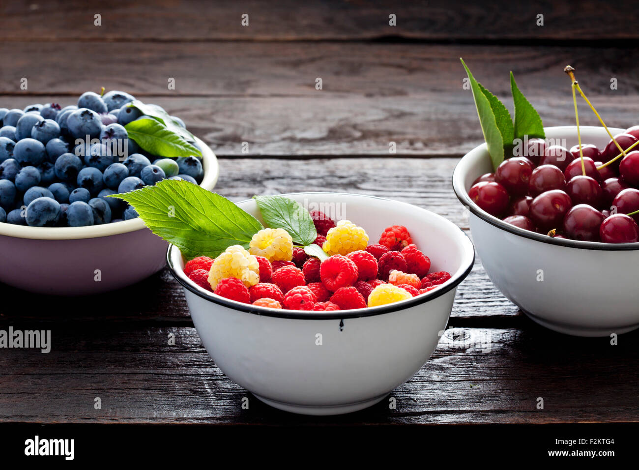 Three bowls sour cherries, raspberries and blueberries on dark wood ...