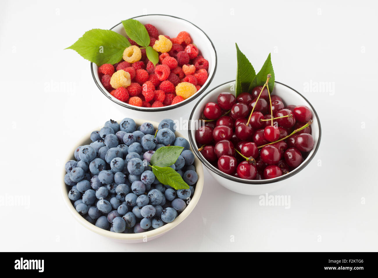 Three bowls of sour cherries, raspberries and blueberries on white ...