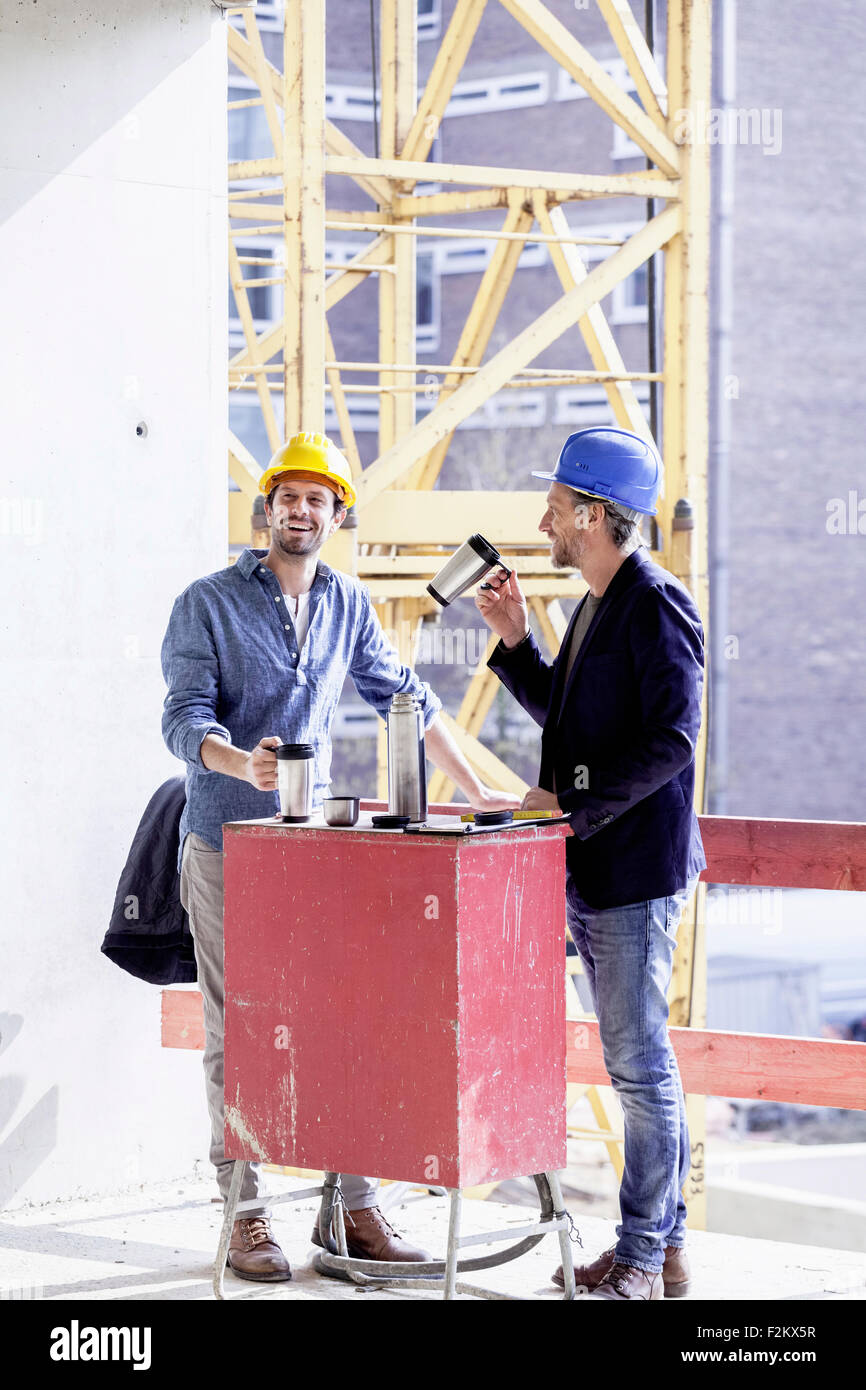 Two men on construction site having coffee break Stock Photo - Alamy