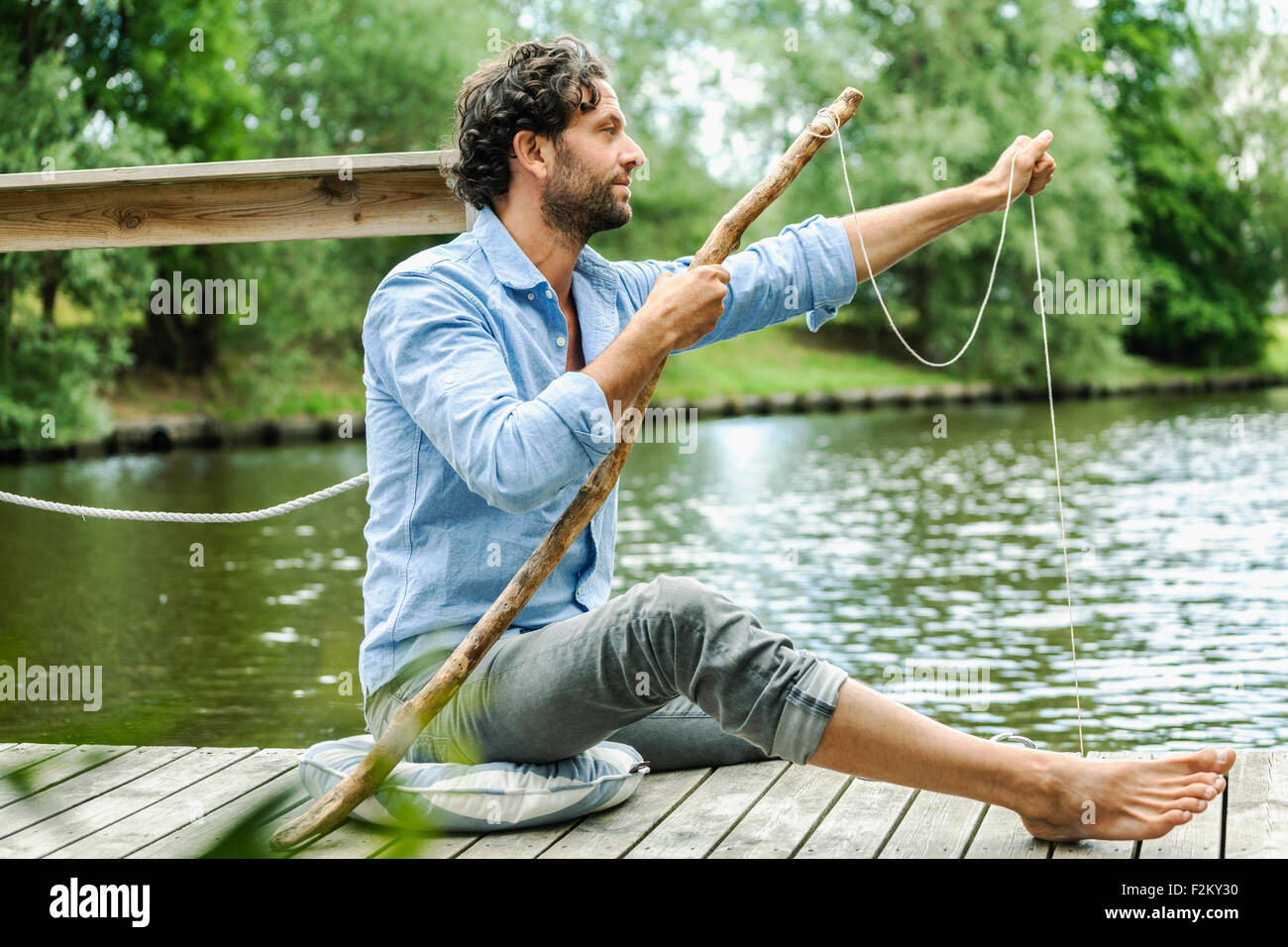 Man sitting on platform at the waterside with selfmade fishing rod ...