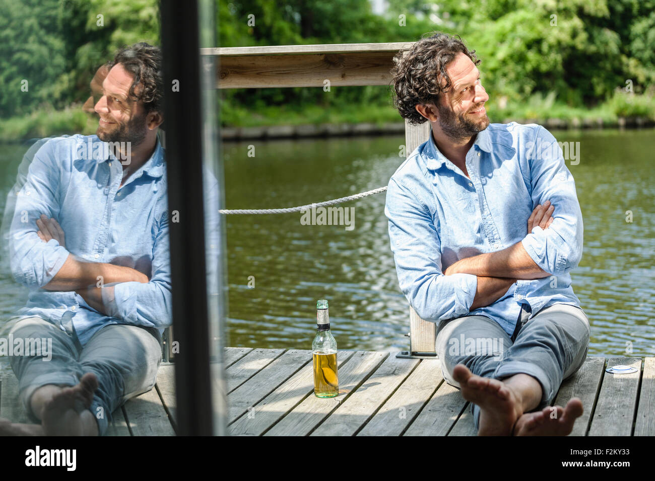 Smiling man sitting on platform at the waterside with beer bottle Stock ...