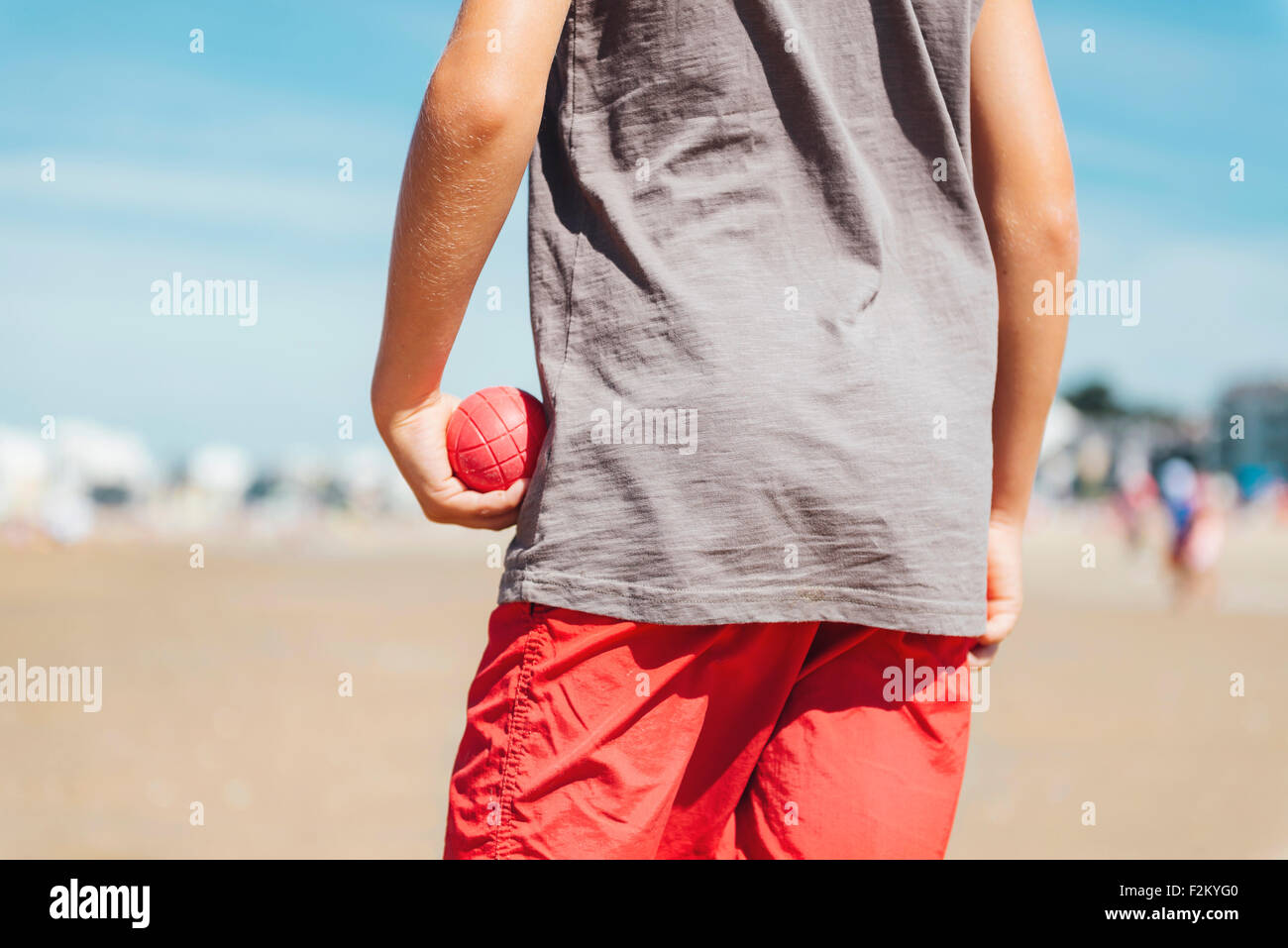 Back view of boy standing on the beach holding red boccia bowl in his ...