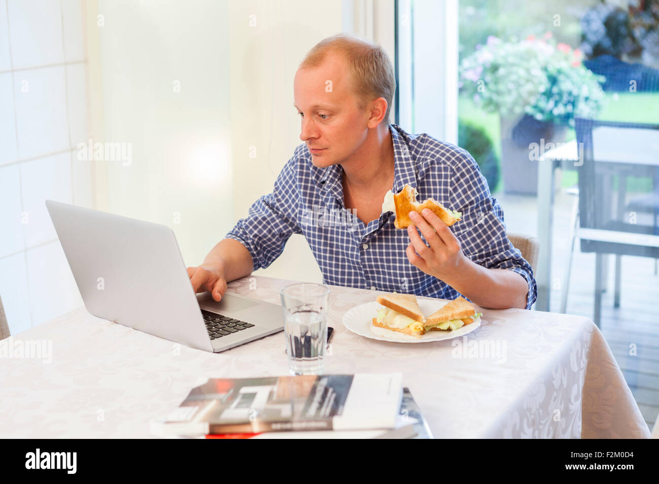 Man at home using his laptop while eating a snack Stock Photo - Alamy