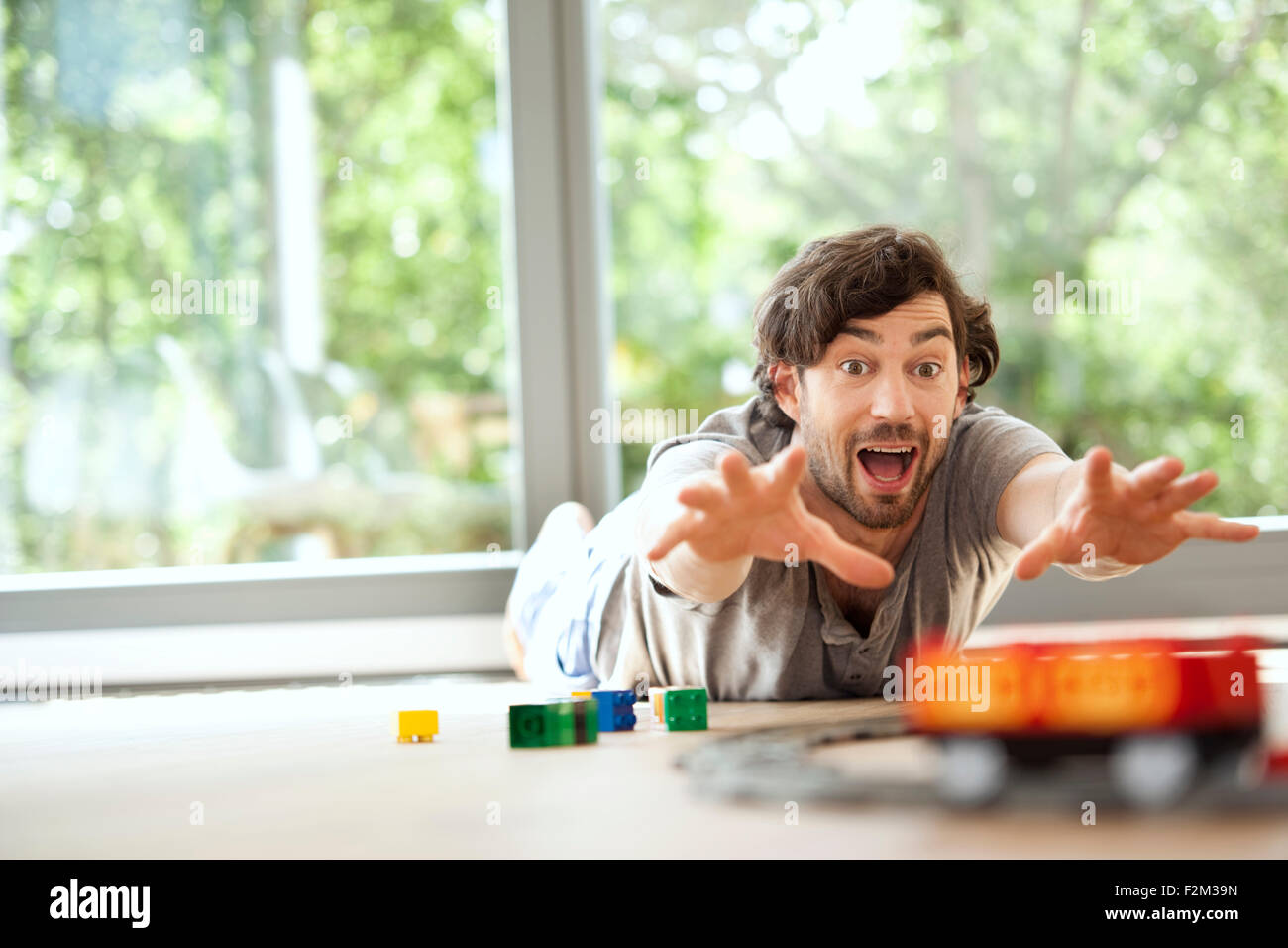Excited man lying on floor reaching out for toy train Stock Photo - Alamy