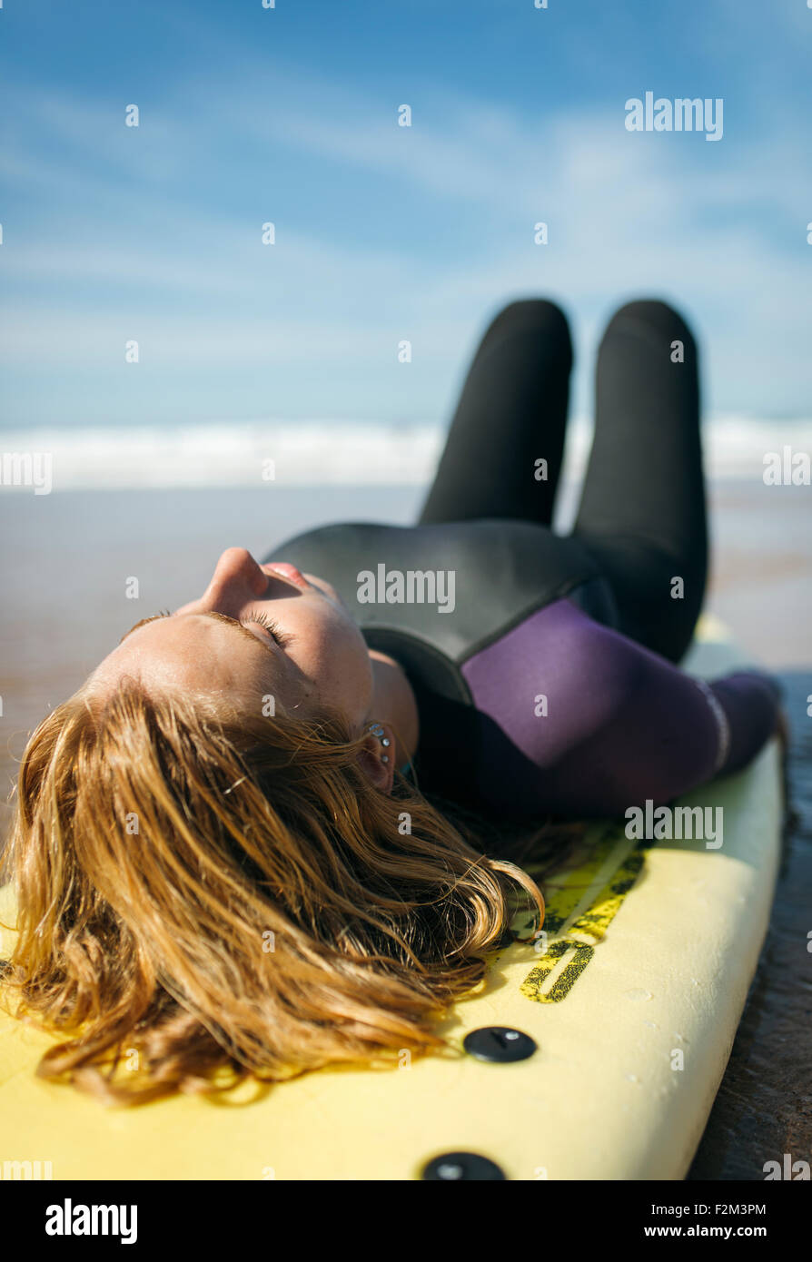 Spain, Colunga, young woman lying on surfboard sunbathing Stock Photo ...