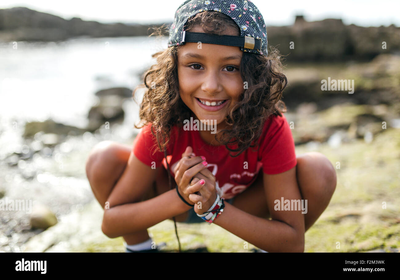 Spain, Gijon, portrait of smiling little girl crouching at rocky coast ...