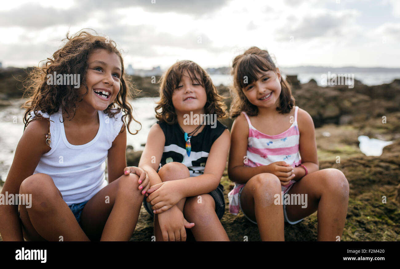 Spain, Gijon, group picture of three little children sitting at rocky ...