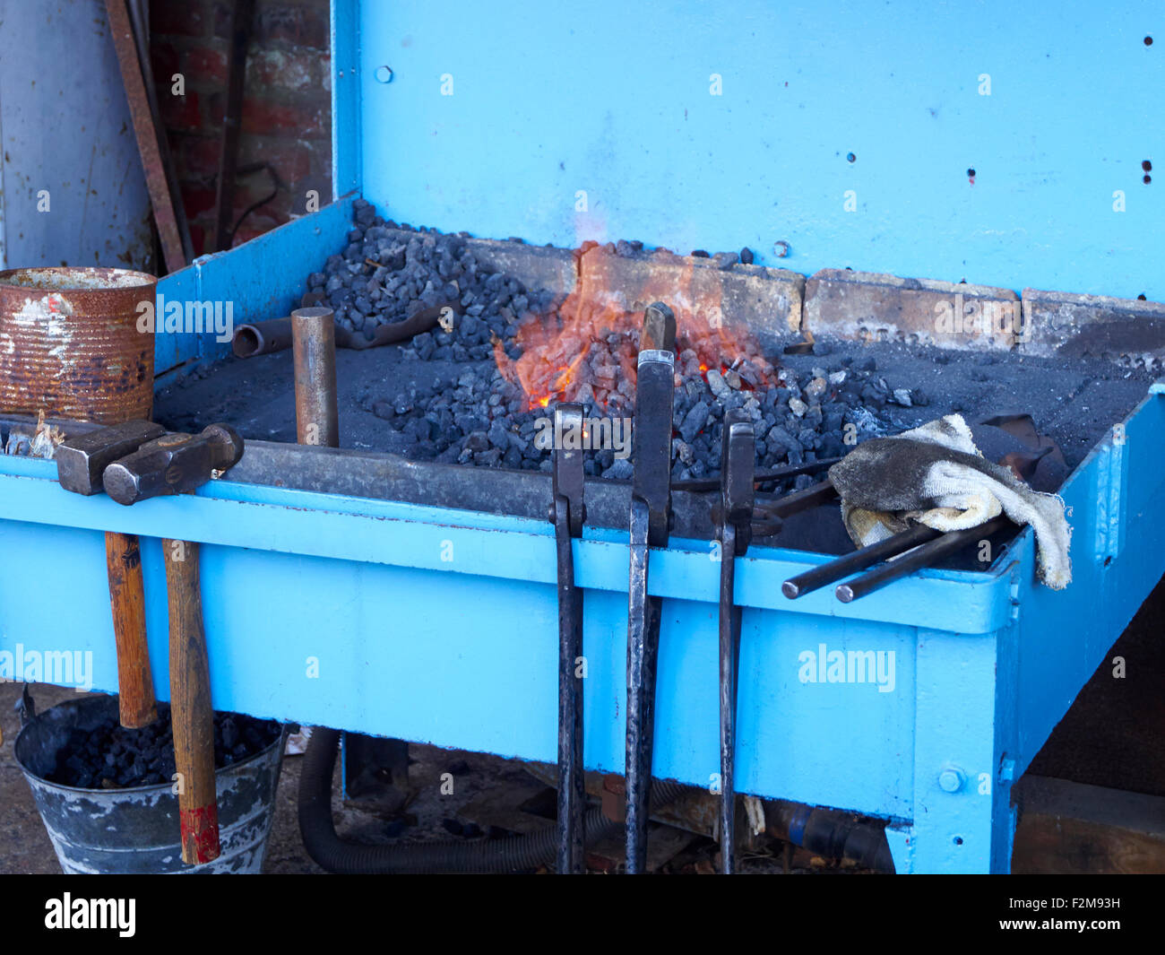 A modern blacksmith's forge with red hot coke heating a piece of iron ...