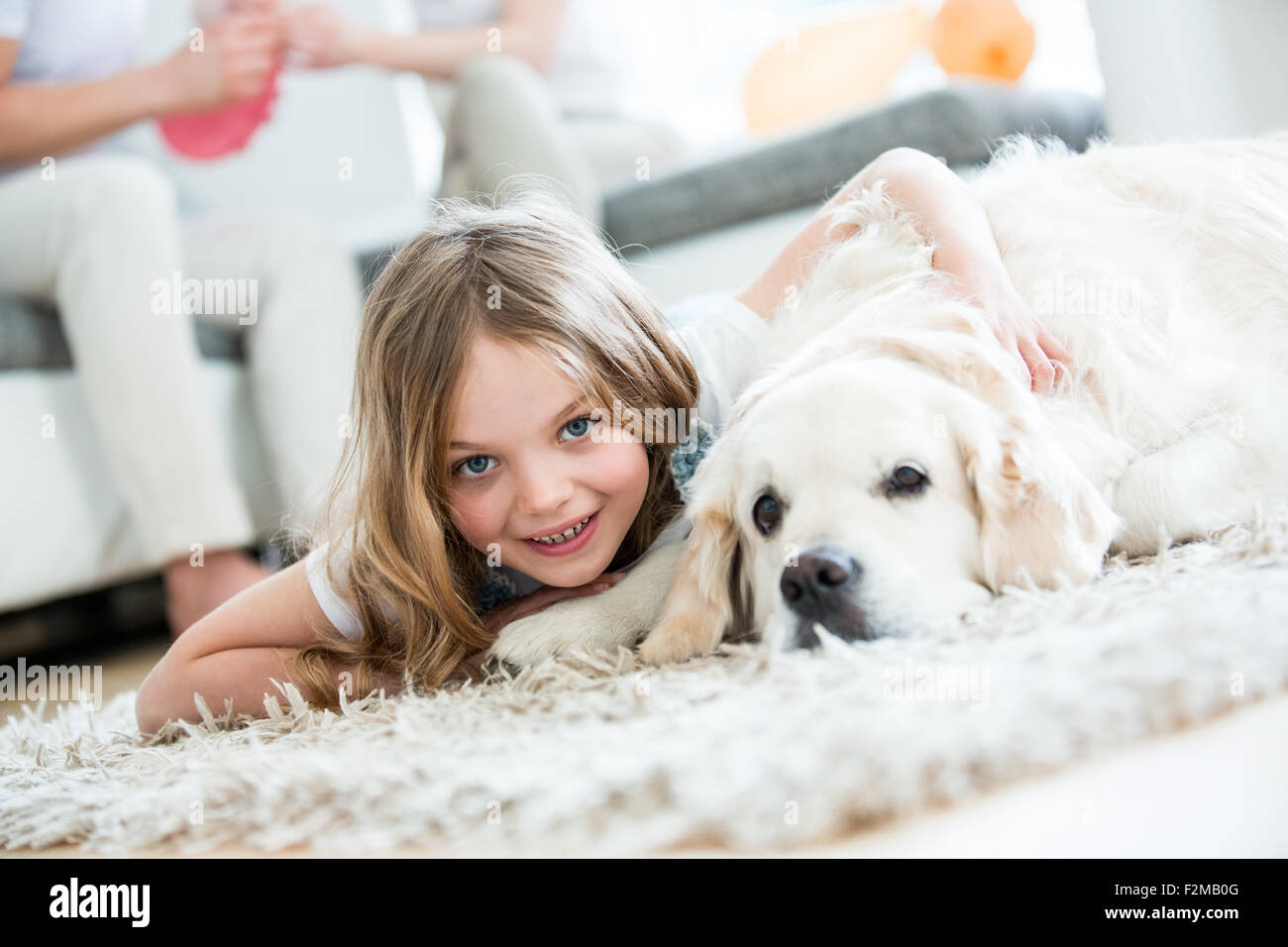 Little girl cuddling with her dog, lying on floor, parents in ...