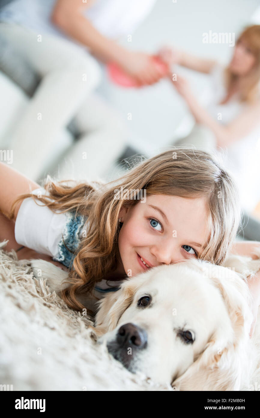Little girl cuddling with her dog, lying on floor, parents in ...