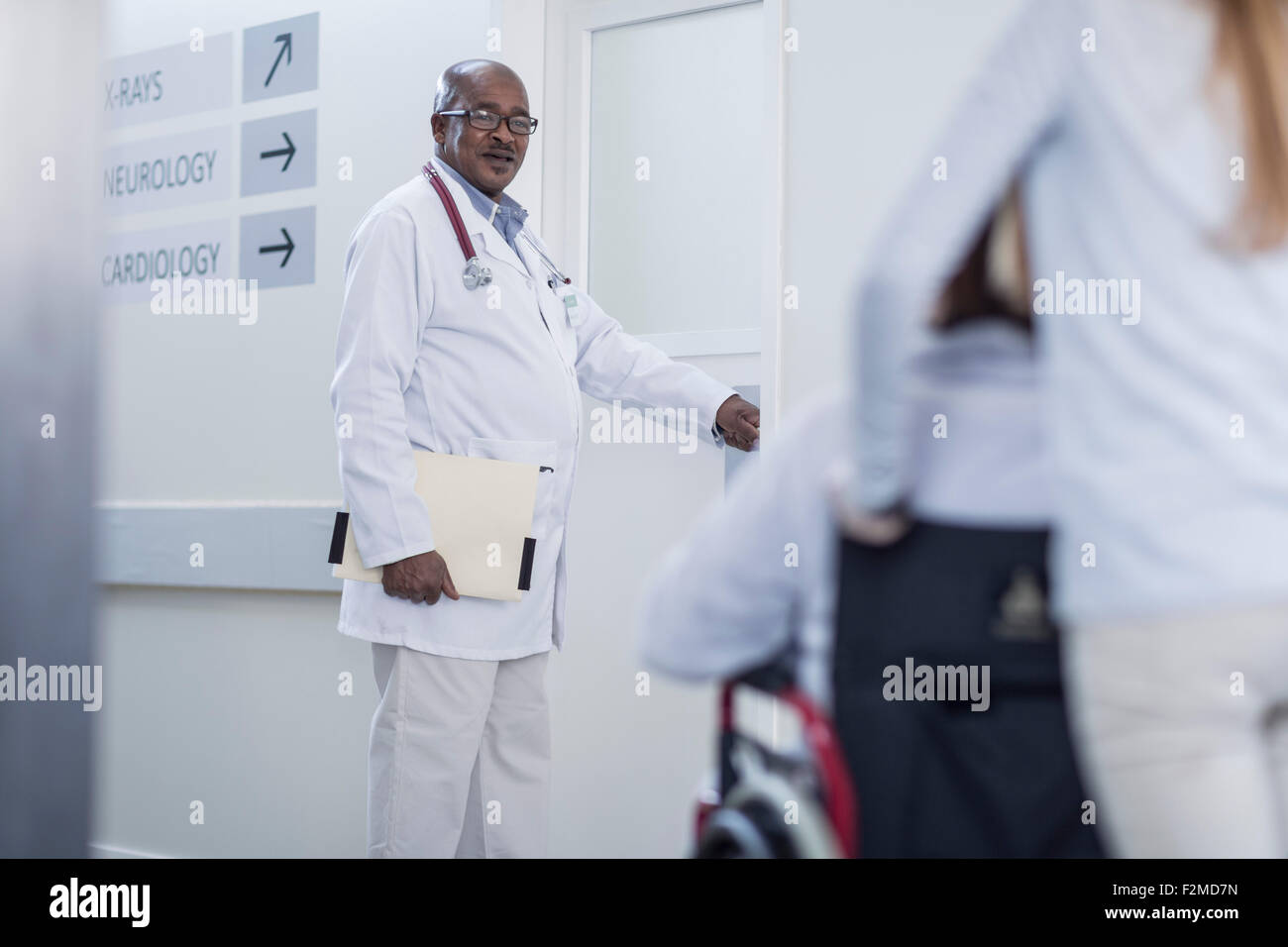 Doctor in hospital corridor opening door and patient in wheelchair ...
