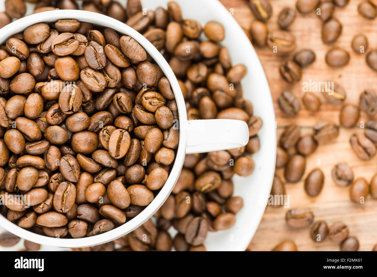 coffee beans inside white half visible cup and plate on wood background ...
