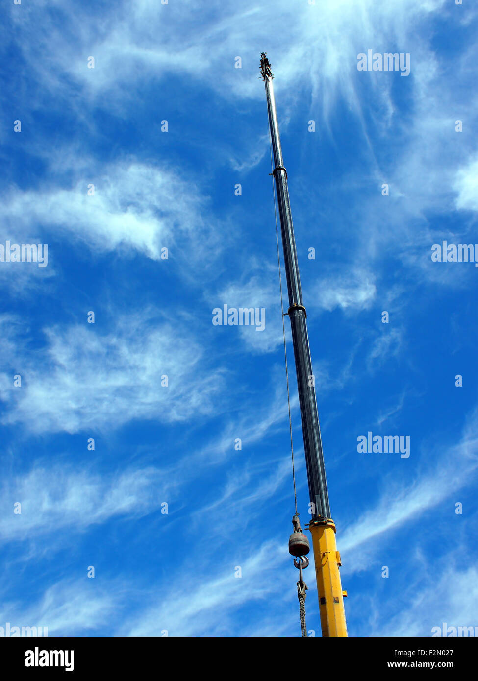 Upward view on the boom of a crane against the blue sky with white ...