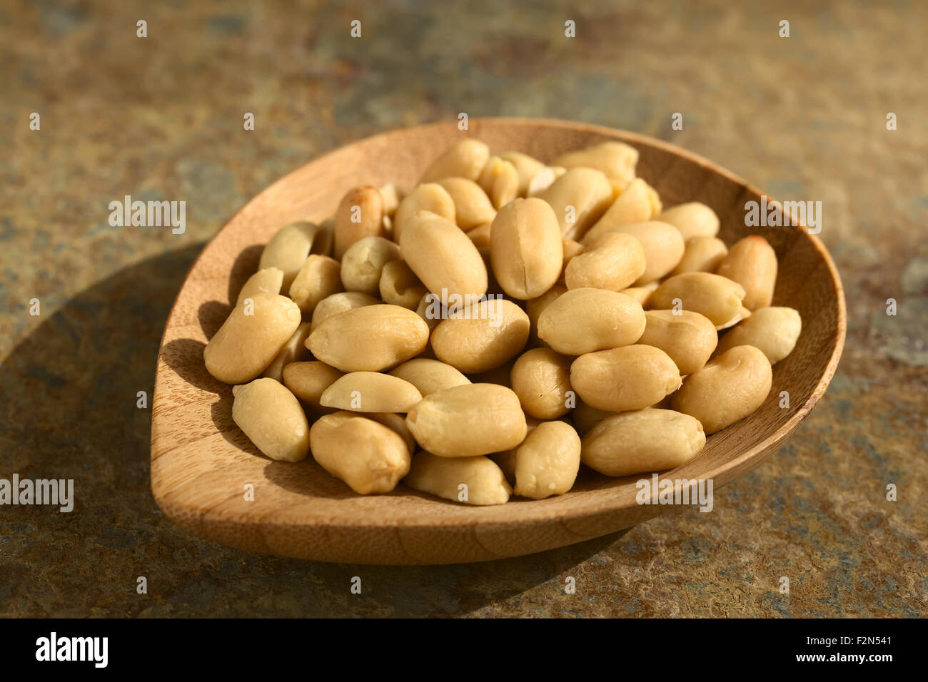 Roasted peeled unsalted peanuts on small bamboo plate, photographed on ...