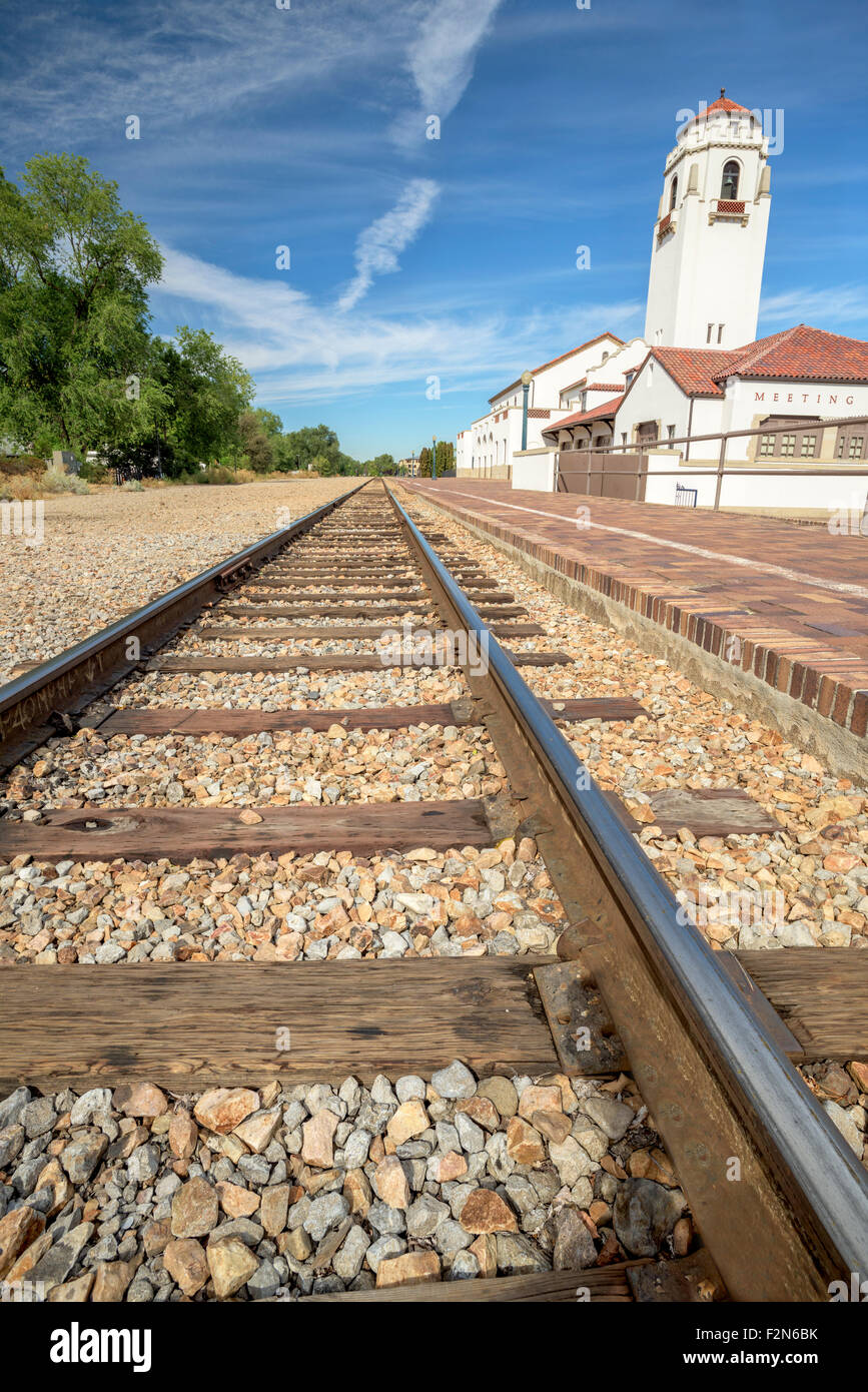 Railroad tracks lead past a depot with blue sky and clouds Stock Photo ...
