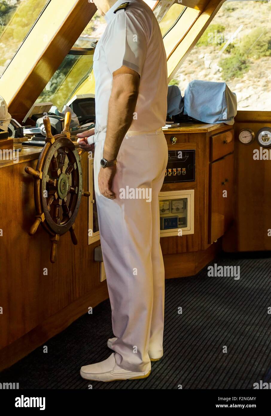 View of a captain in uniform steering the wheel directing the ship into ...
