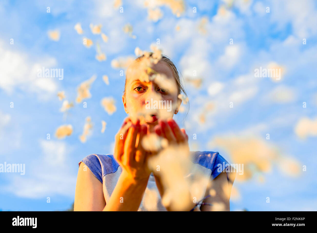 Caucasian teenage girl blowing flower petals under blue sky Stock Photo ...