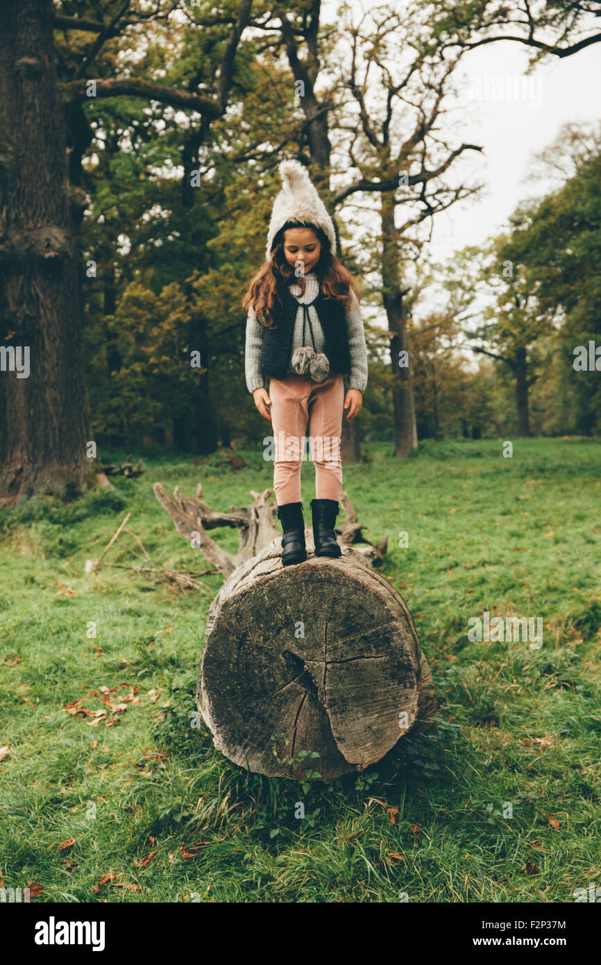 Little girl wearing cap standing on a tree trunk in autumnal park Stock ...
