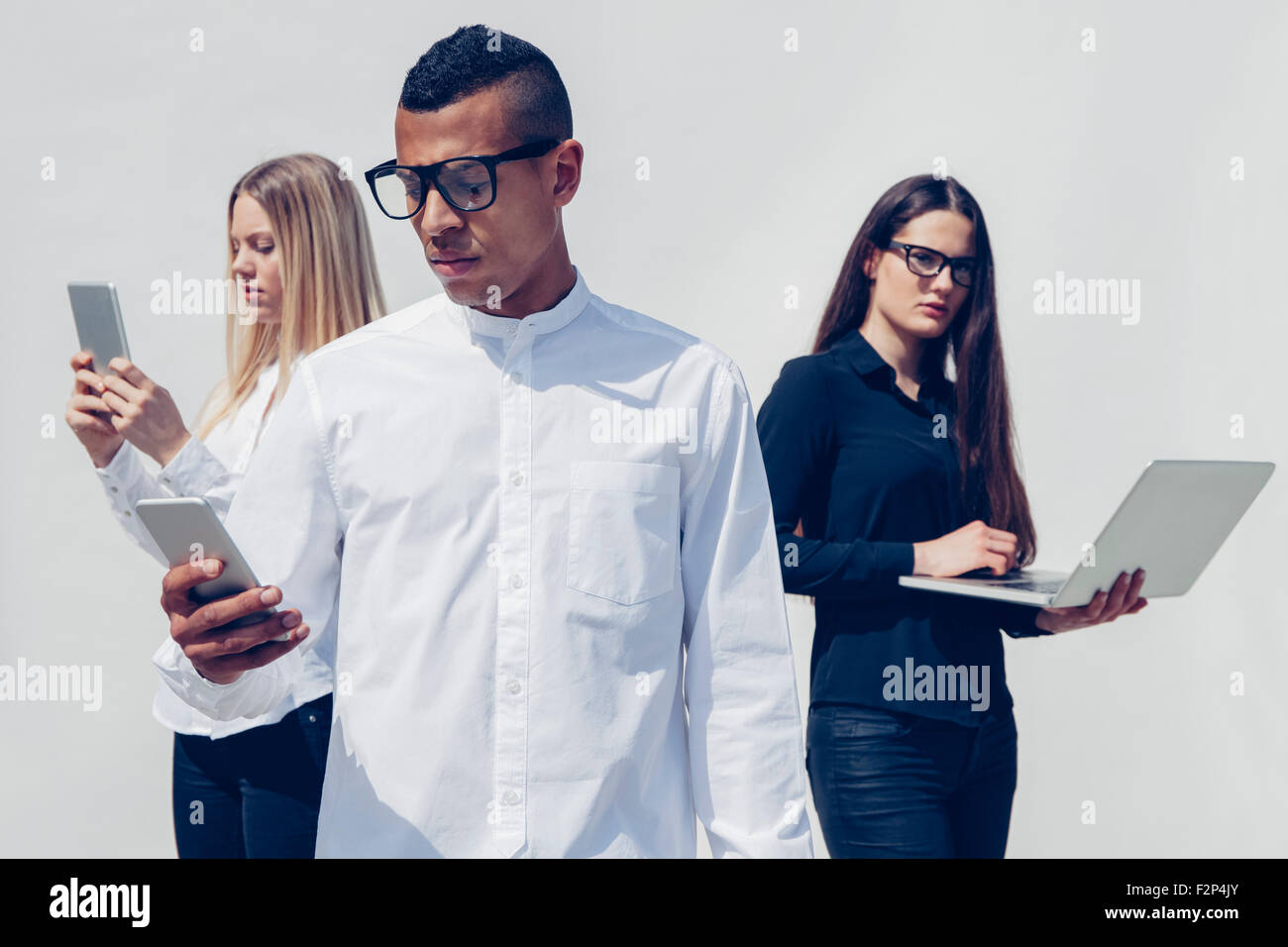 Three stylish young people with mini tablet, smartphone and laptop in ...