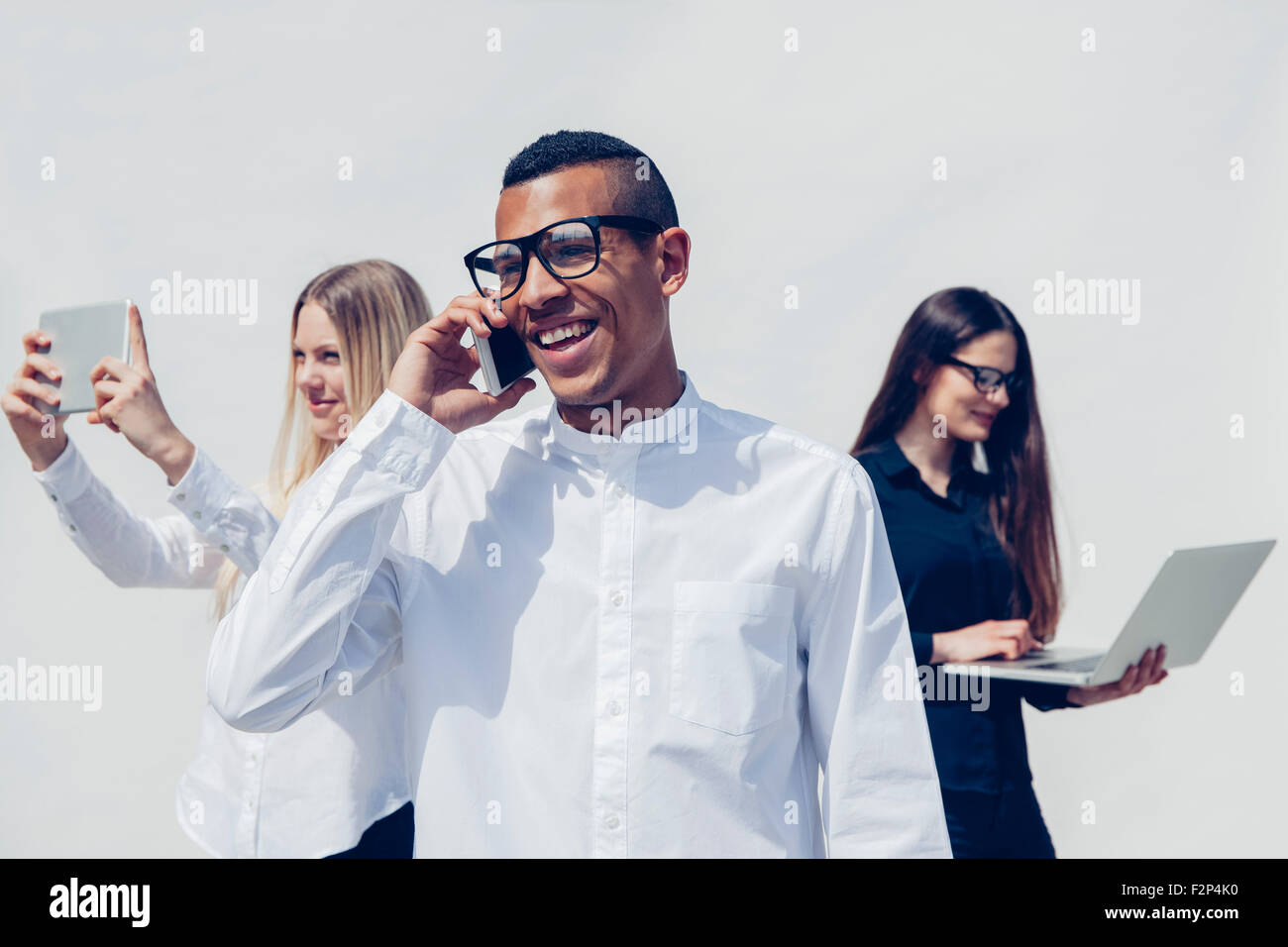 Three stylish young people with mini tablet, smartphone and laptop in ...