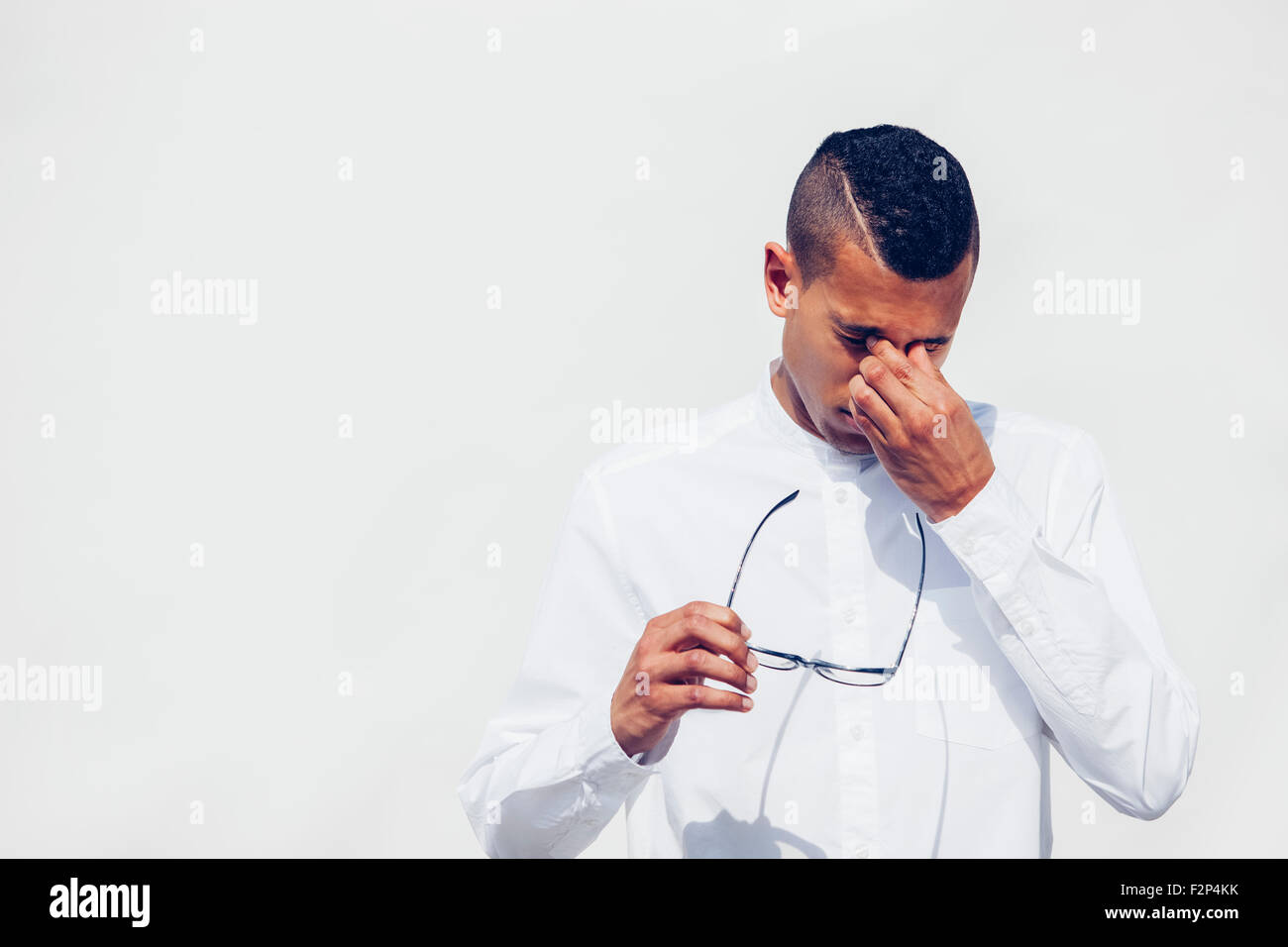 Young man with shaved hair holding glasses in his hand while rubbing ...