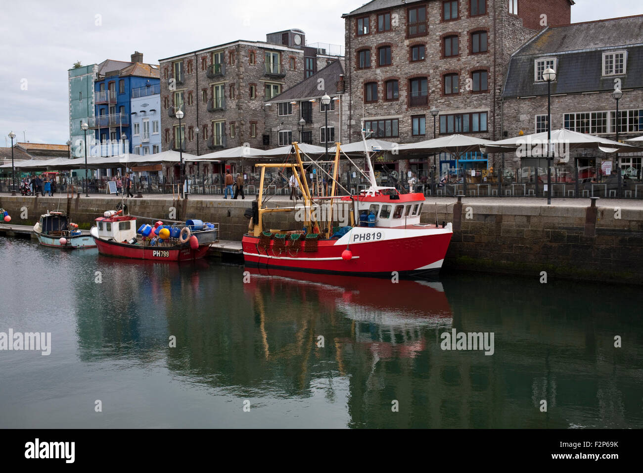 fishing boats moored in the Sutton harbour, Plymouth, UK with the shops ...