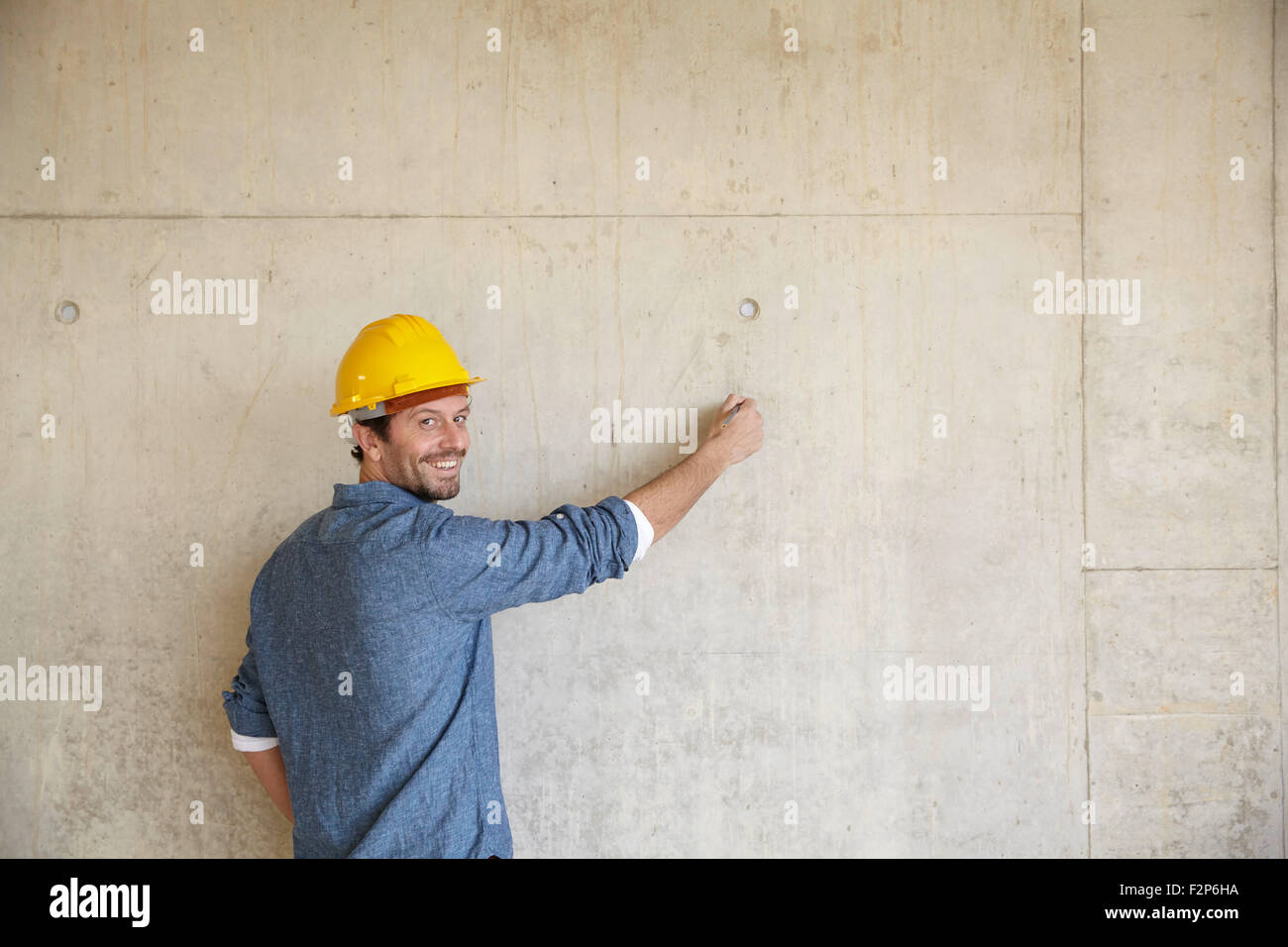 Smiling man with hard hat on construction site drawing on concrete wall ...