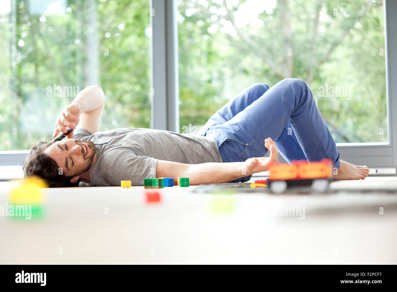 Smiling man on cell phone lying on floor next to toy train Stock Photo ...