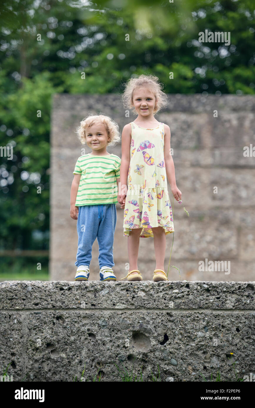 Portrait of little sister and brother standing side by side on a wall ...