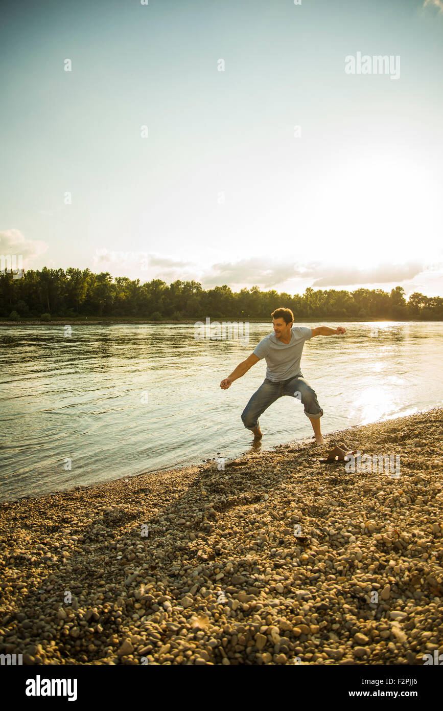 Man standing at riverside throwing pebbles into the water Stock Photo ...