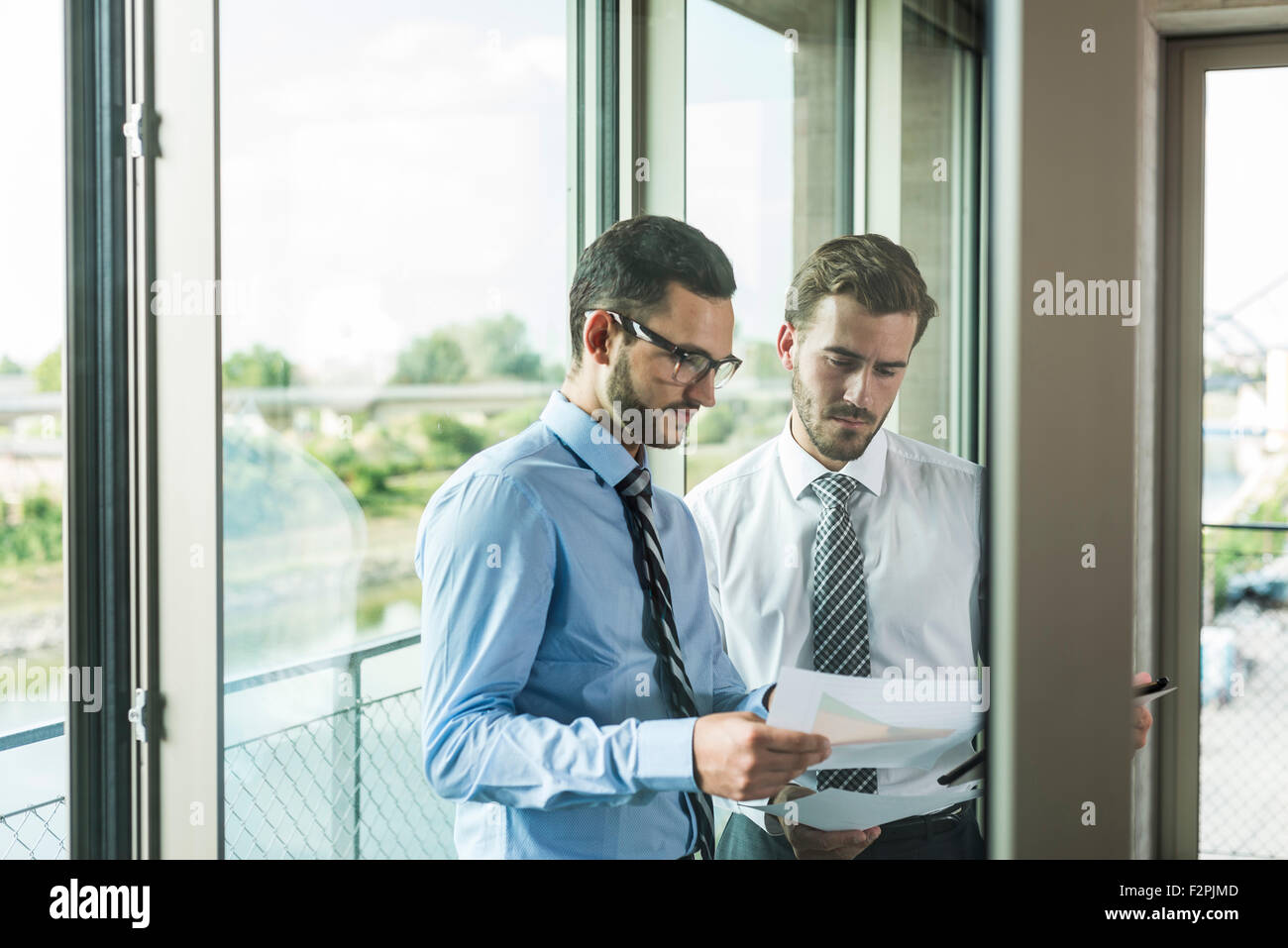 Two young businessmen looking at documents at the window Stock Photo ...