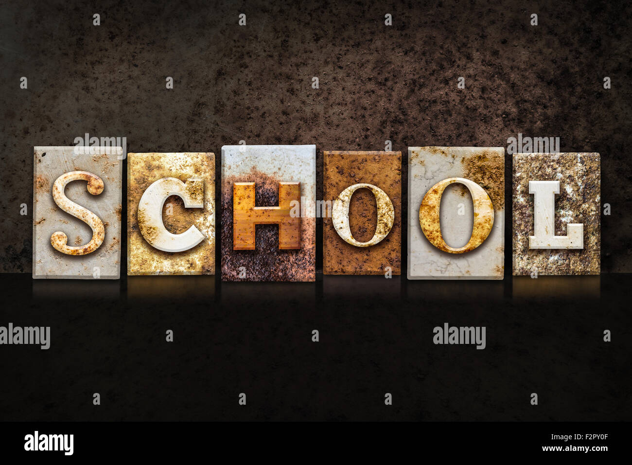 The word "SCHOOL" written in rusty metal letterpress type on a dark ...