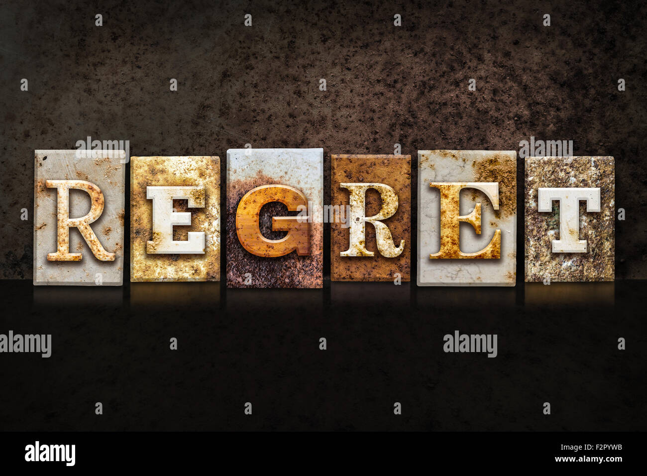 The word "REGRET" written in rusty metal letterpress type on a dark ...