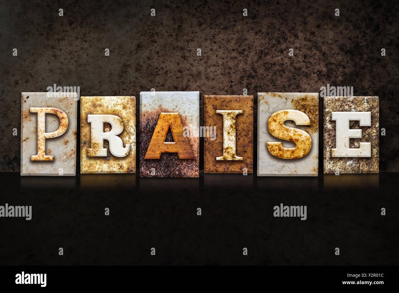 The word "PRAISE" written in rusty metal letterpress type on a dark ...