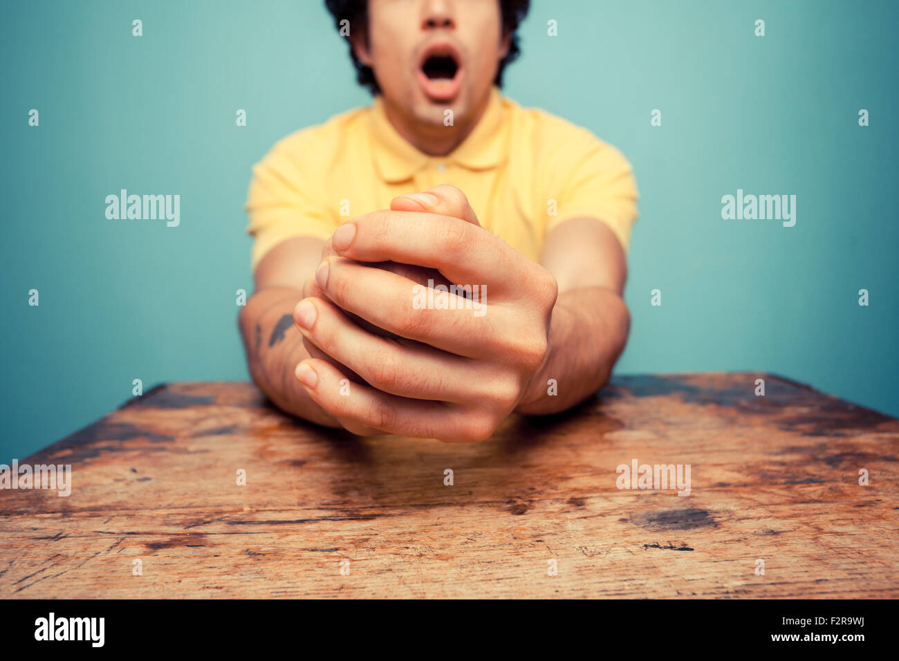Surprised young man at table with his hands folded Stock Photo - Alamy