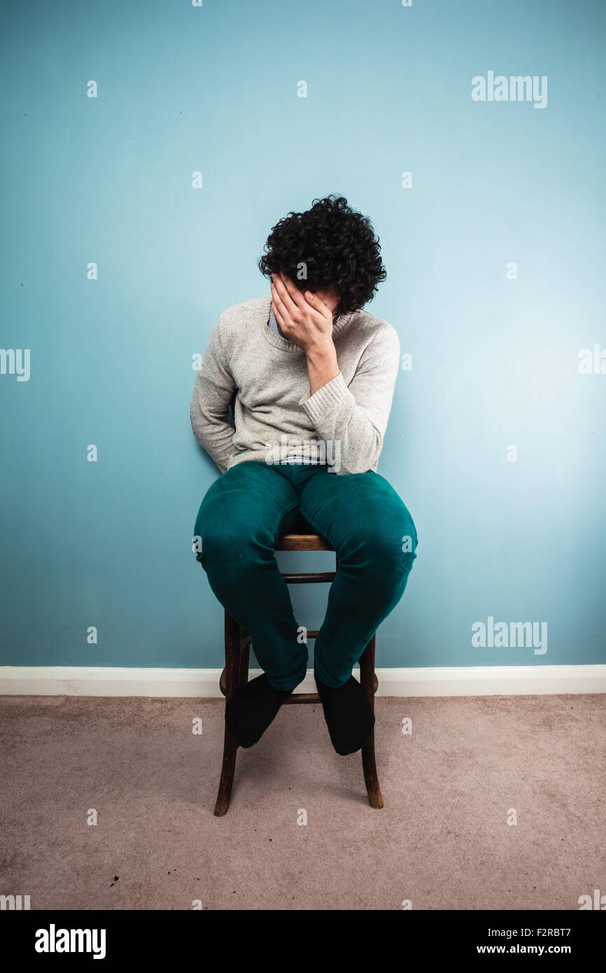 A sad young man is sitting on a high chair by a blue wall Stock Photo ...