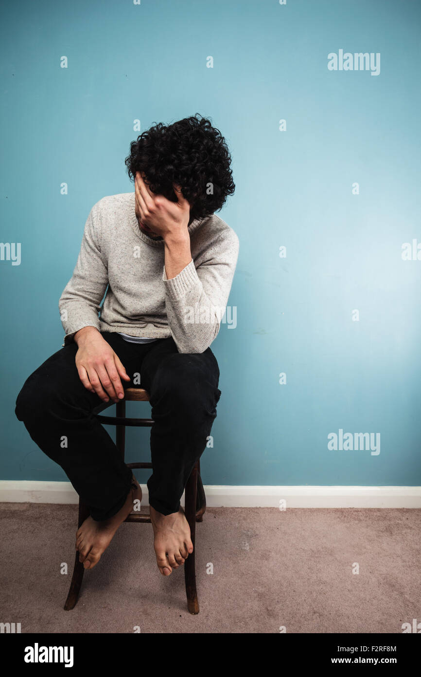 A sad young man is sitting on a high chair by a blue wall Stock Photo ...