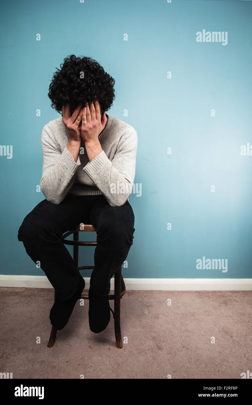 A sad young man is sitting on a high chair by a blue wall Stock Photo ...
