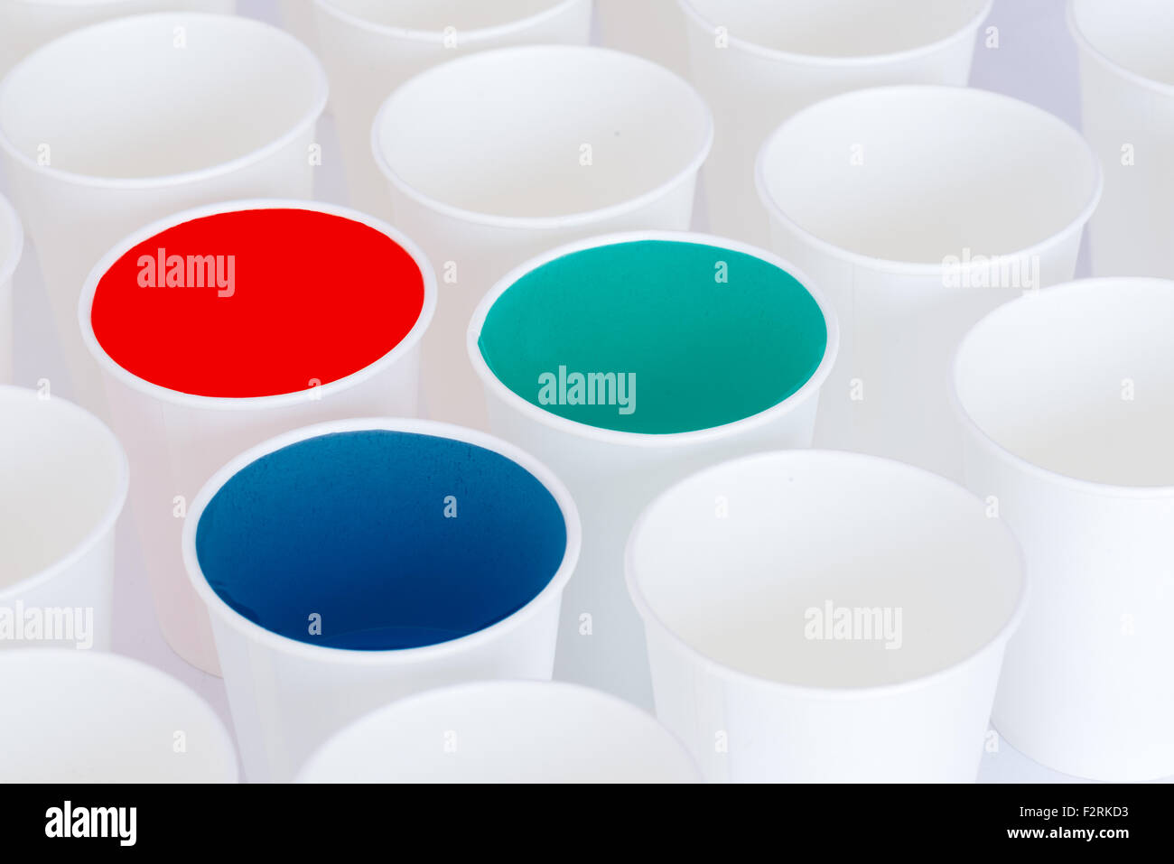 White paper cups on a white background. Some cups have colored liquid ...